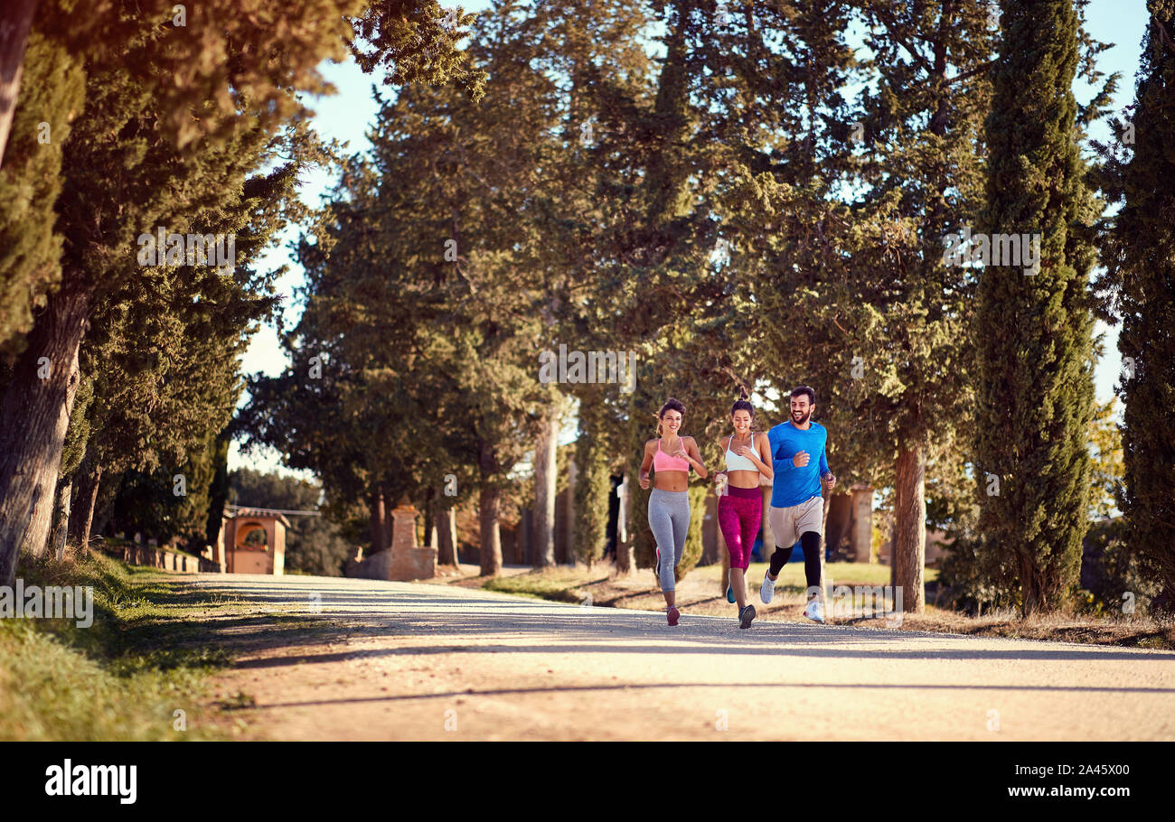 smiling people running together in nature. Young friends exercising ...
