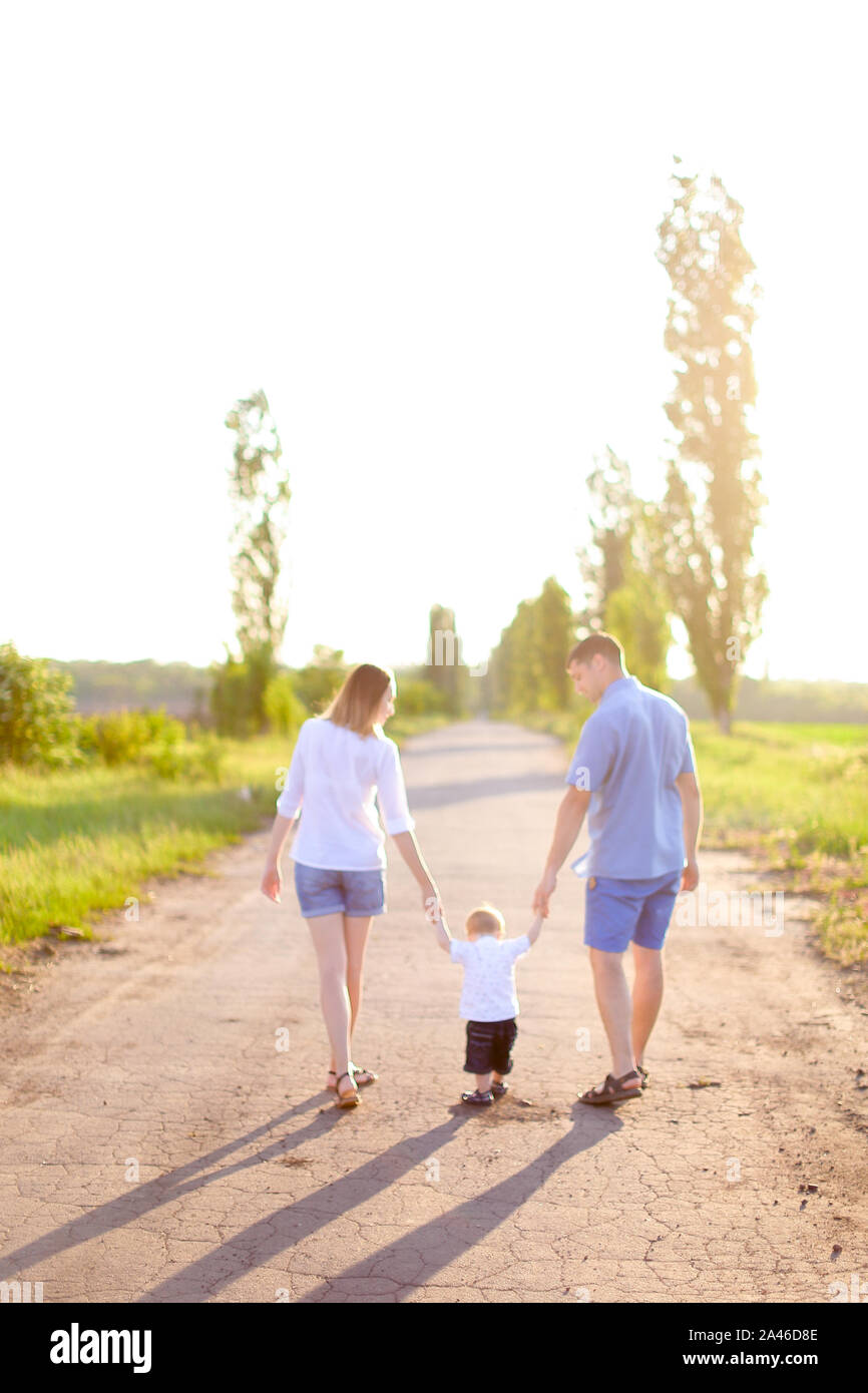 Back view of young mother and father walking on road with little baby ...
