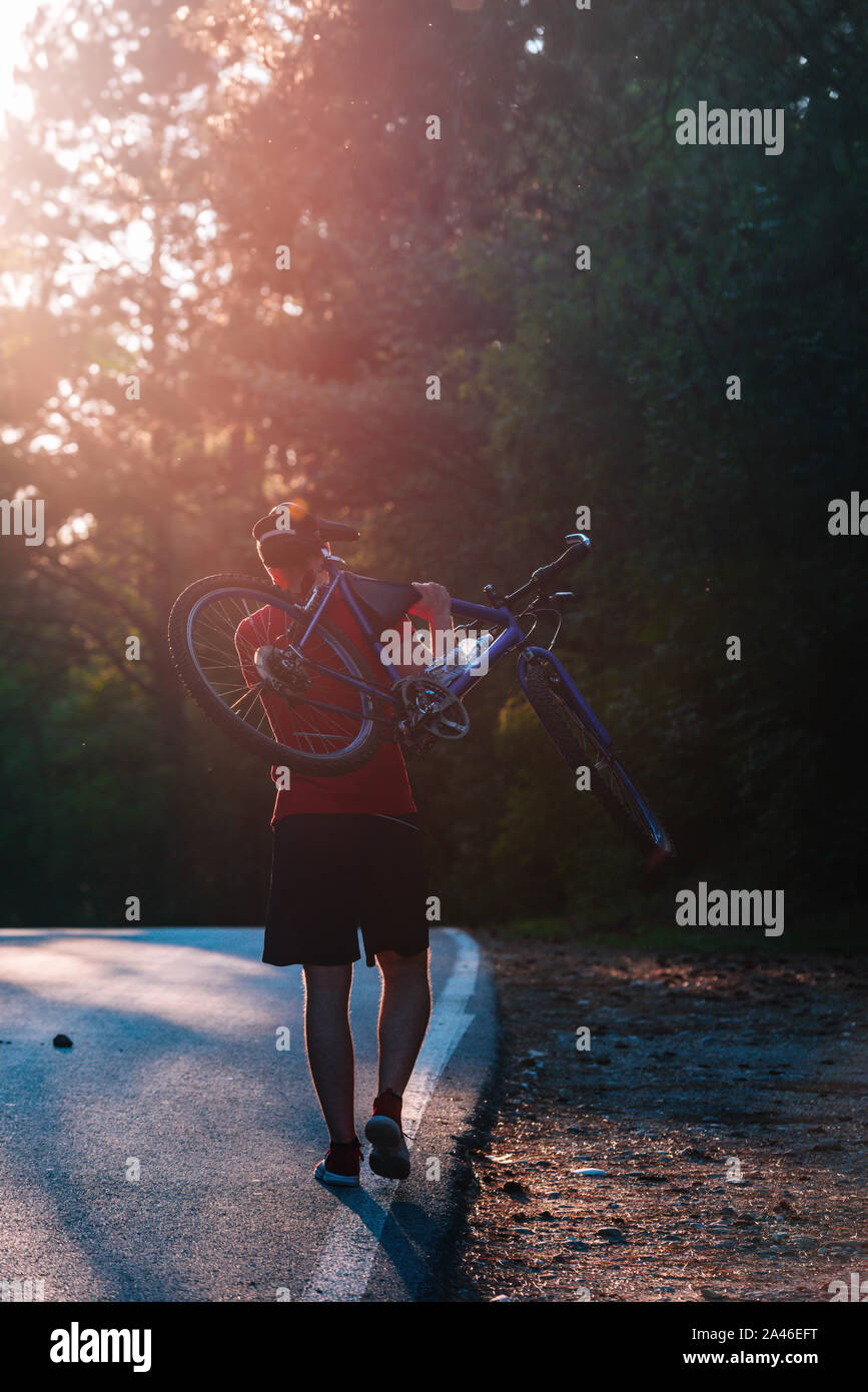 Strong athlete cyclist ( biker ) carrying his bicycle on his back on an ...