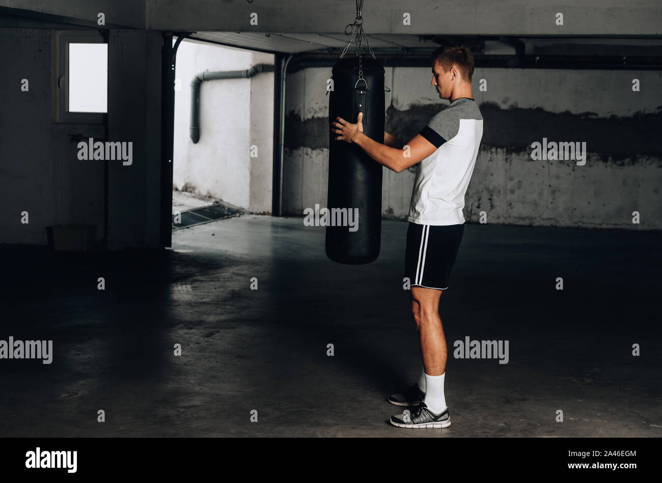 Sporty man set up boxing bag on the wall in underground garage Stock ...