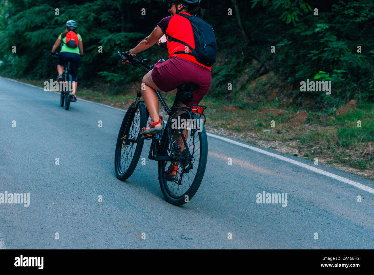 Male cyclist riding his bike on sunset on a road through deep woods ...