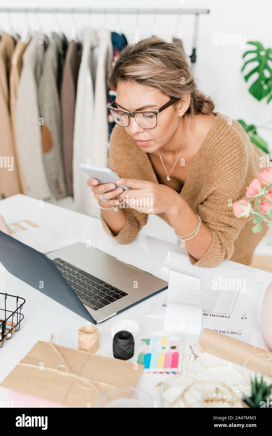 Pretty young casual shop assistant of modern boutique bending over ...