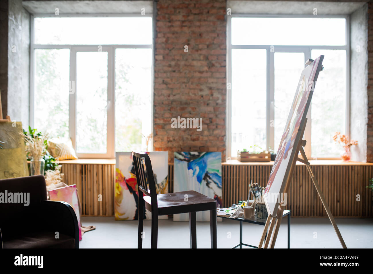 Wooden chair of painter, easel with unfinished painting and other arts ...