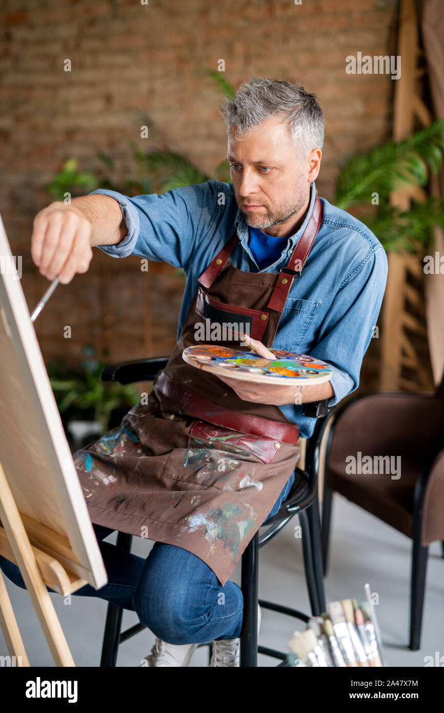 Concentrated professional painter with palette working over new ...