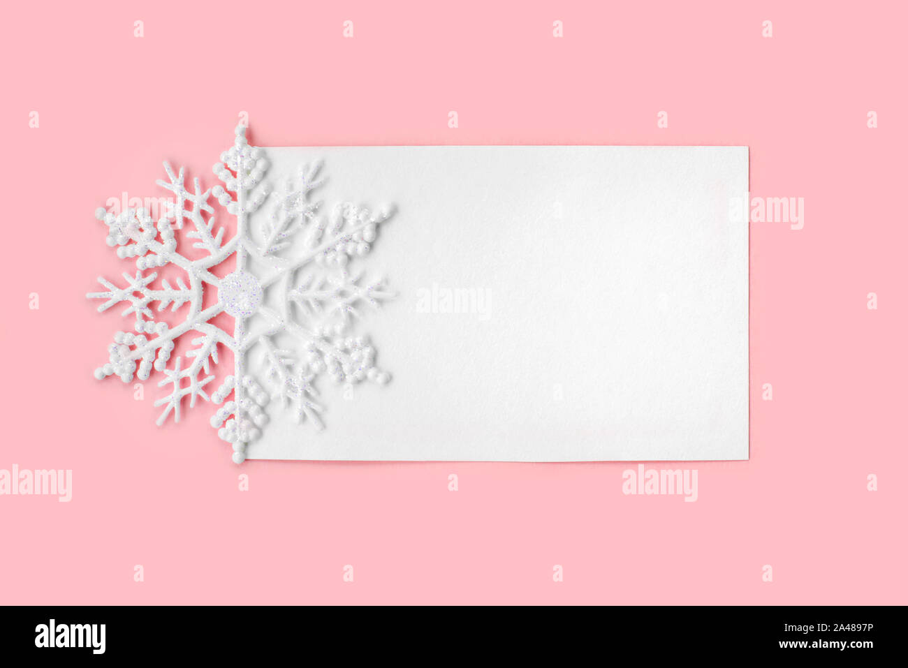 White paper card decorated with snowflake on pink background. New Year ...