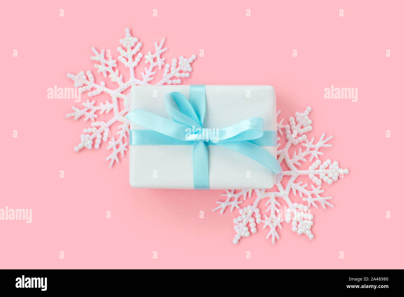 White gift box decorated with snowflakes on pink background. New Year ...