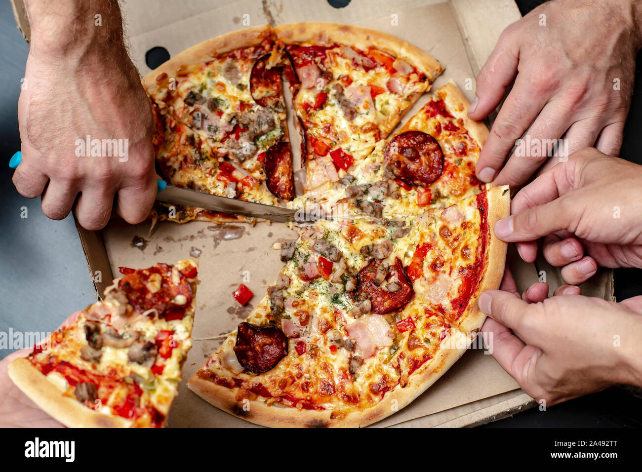 House party. Man's hand cuts the pizza and happy friends snapping a ...