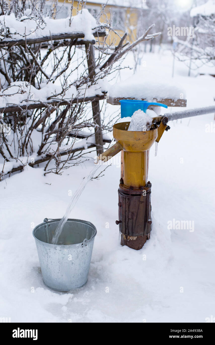 Pour clean drinking water into a bucket using a water pump, on a frosty ...