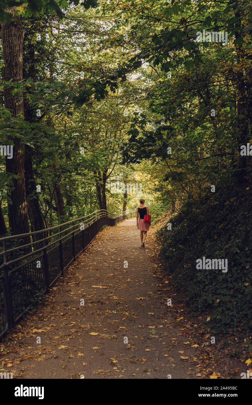 A girl walking on a path with fallen leaves on a sunny fall day in a ...