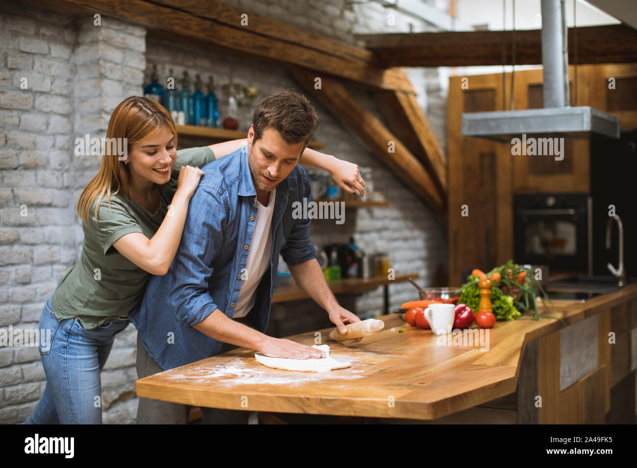 Cheerful young couple making pizza in rustic kitchen together Stock ...
