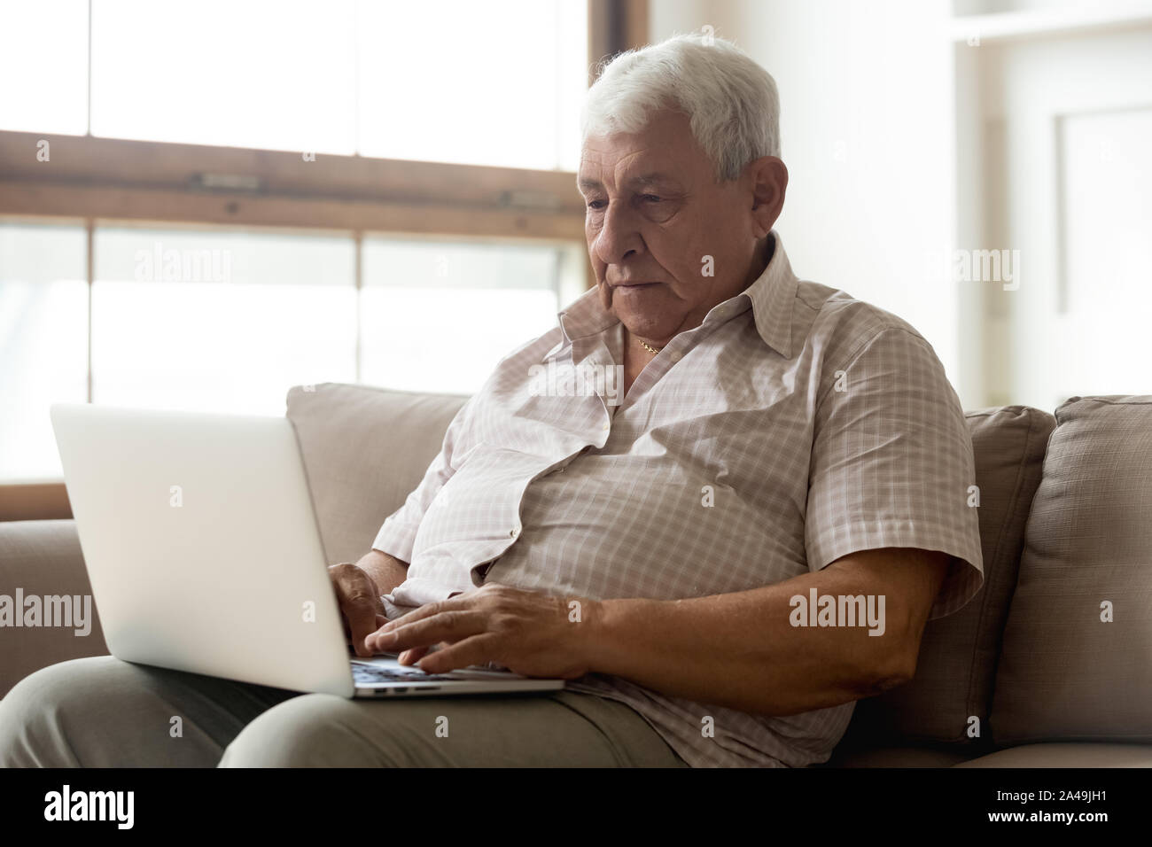 70s elderly man seated on couch using laptop Stock Photo - Alamy