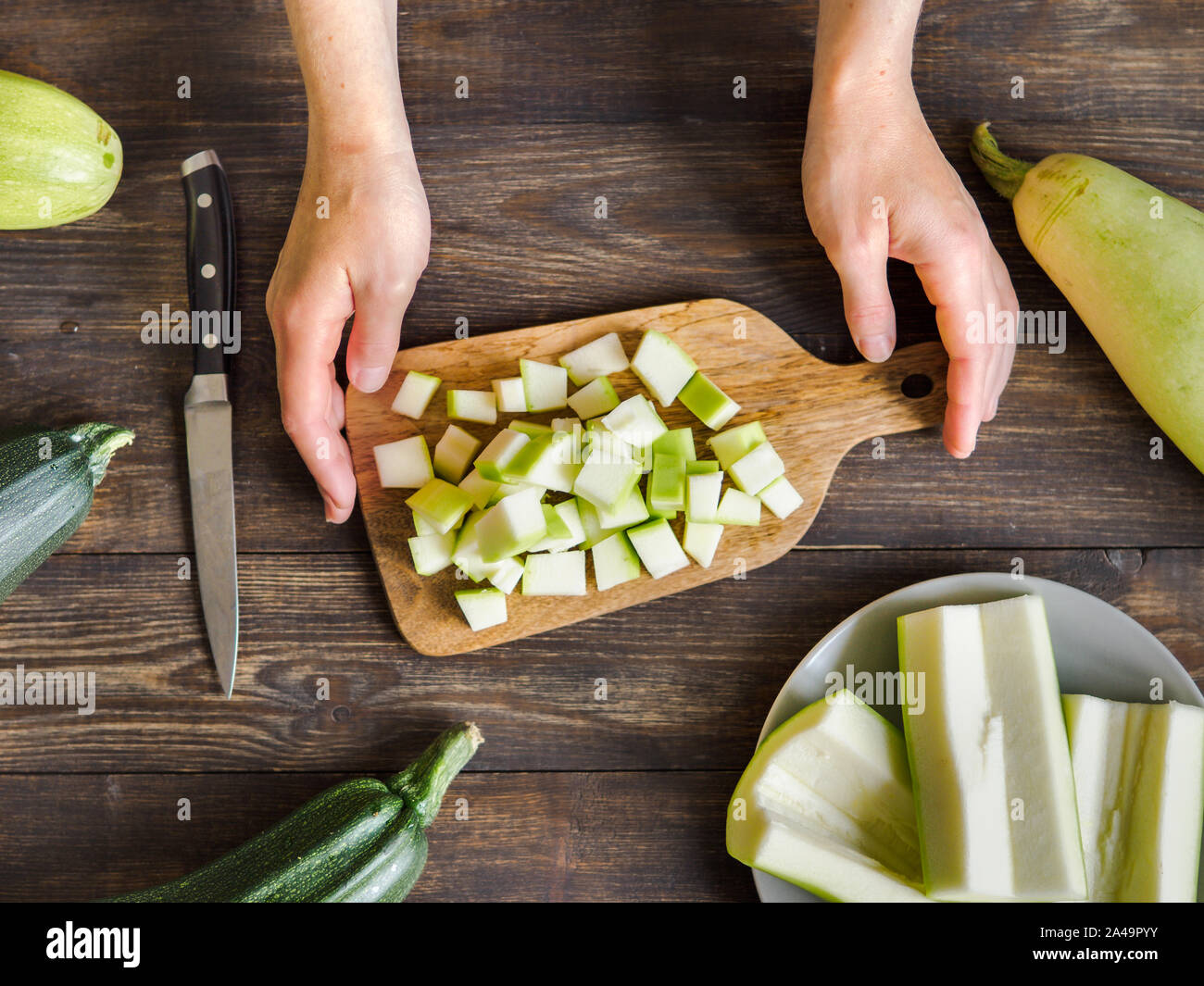 Zucchini harvest. Woman slices zucchini cubes for freezing on wooden ...