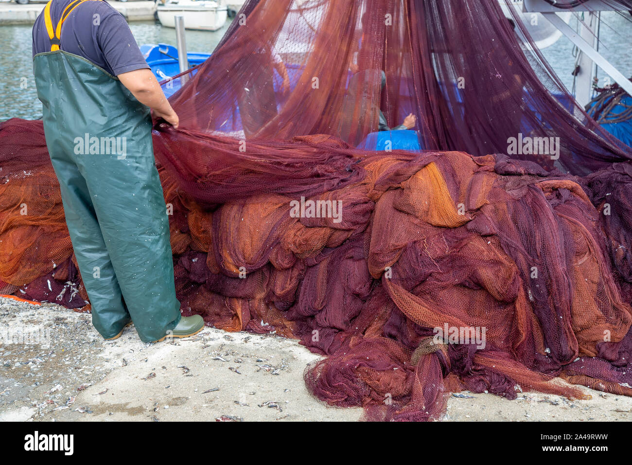 Fisherman cleaning nets and spread on the ground of a fishing port ...