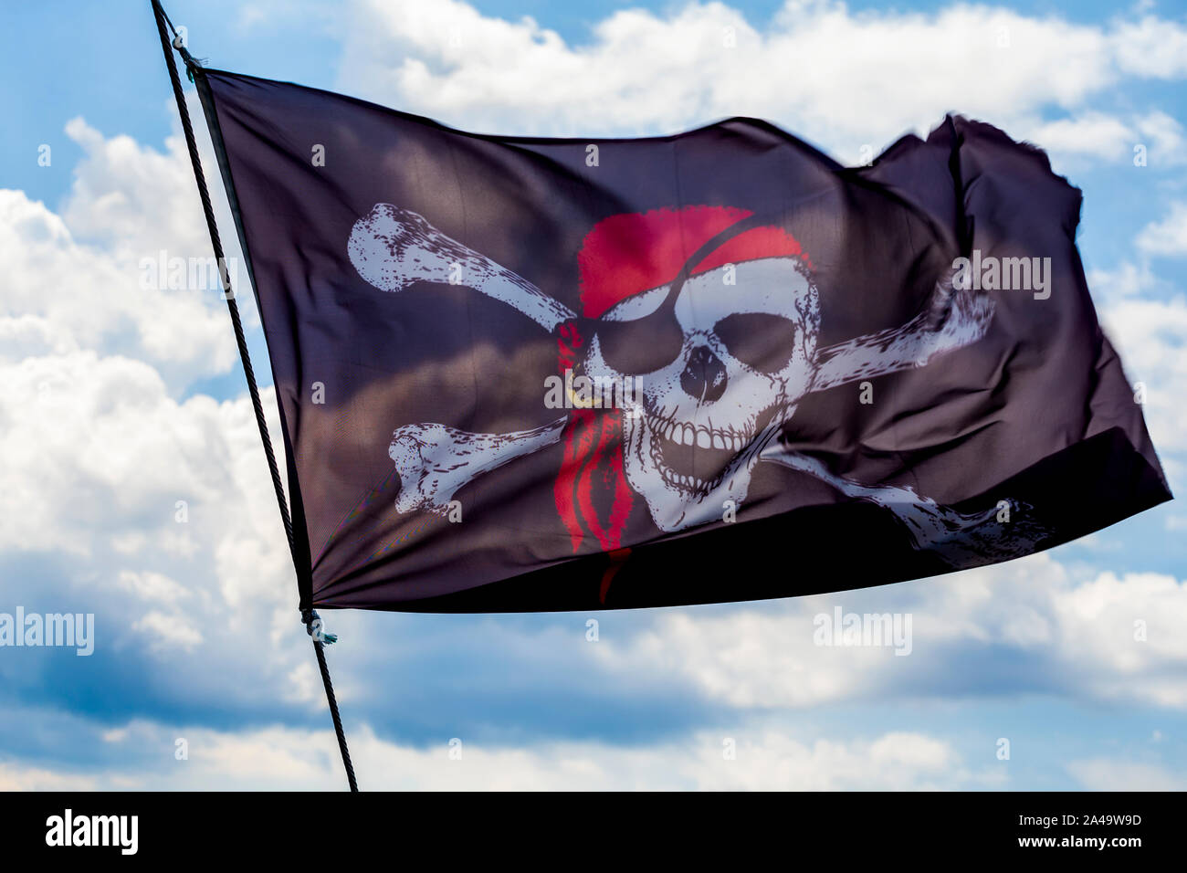 Pirate flag waving on the wind with a blue sky background, skull and ...