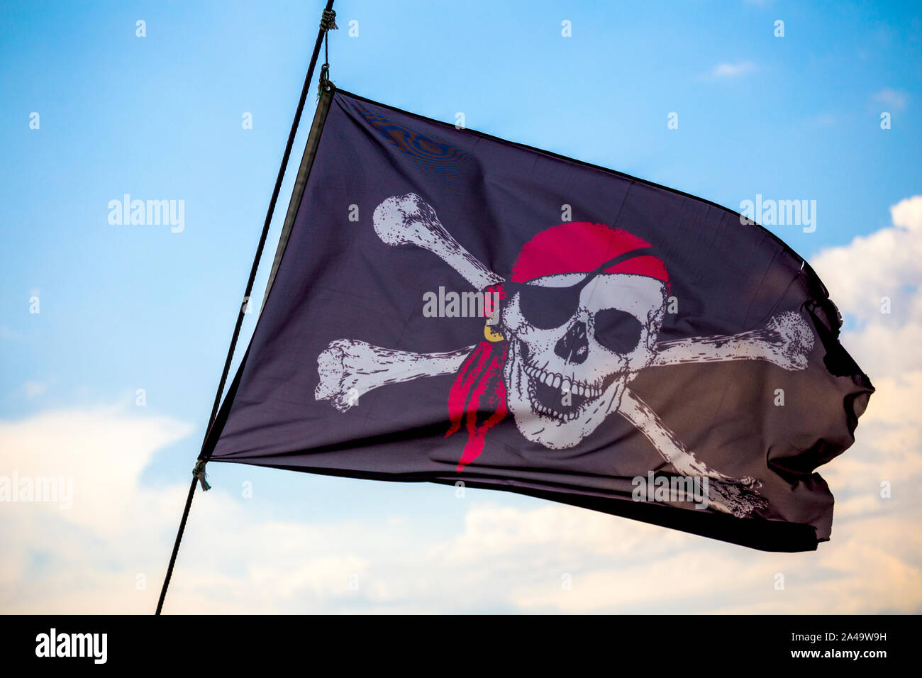 Pirate flag waving on the wind with a blue sky background, skull and ...
