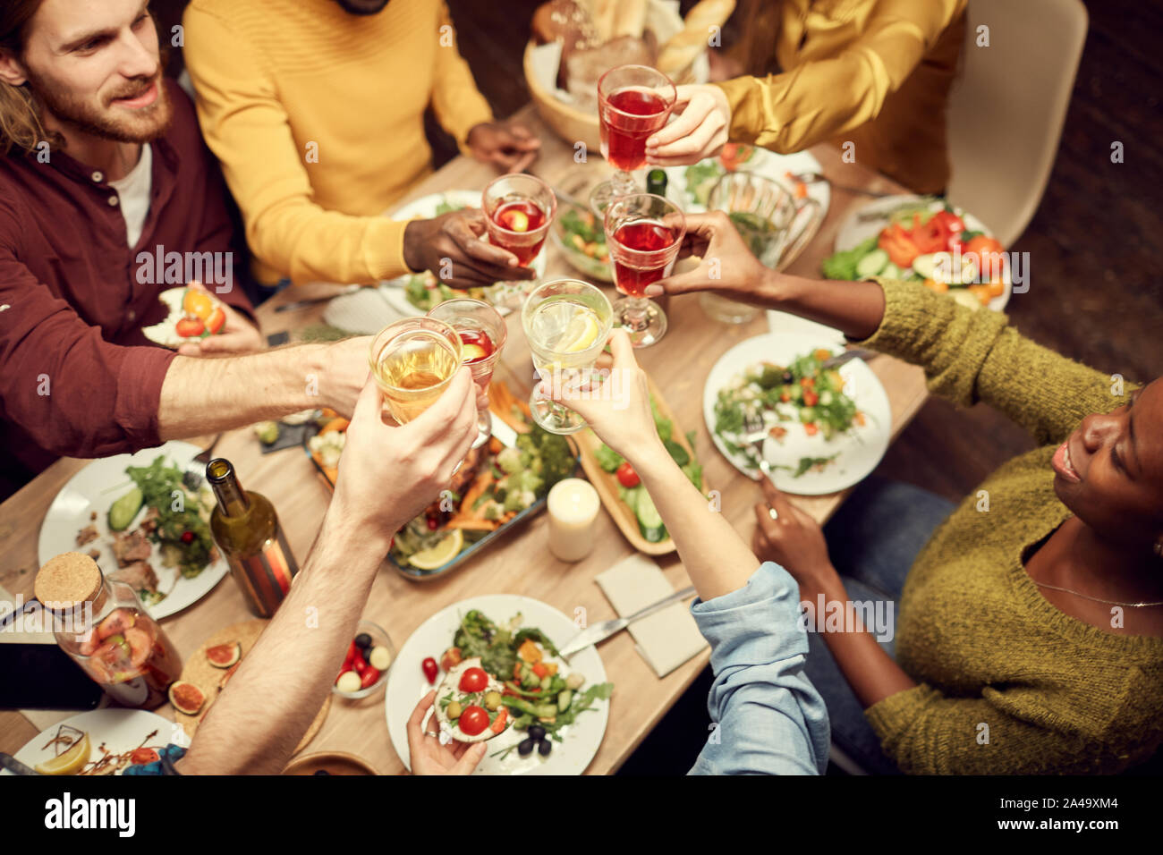 Top view of people raising glasses over dinner table while enjoying ...