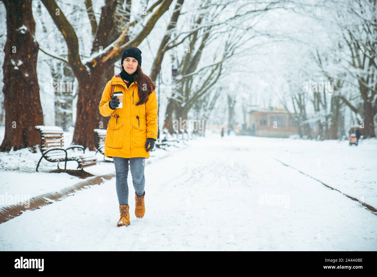 woman walking by snowed city park with thinking face with coffee cup ...