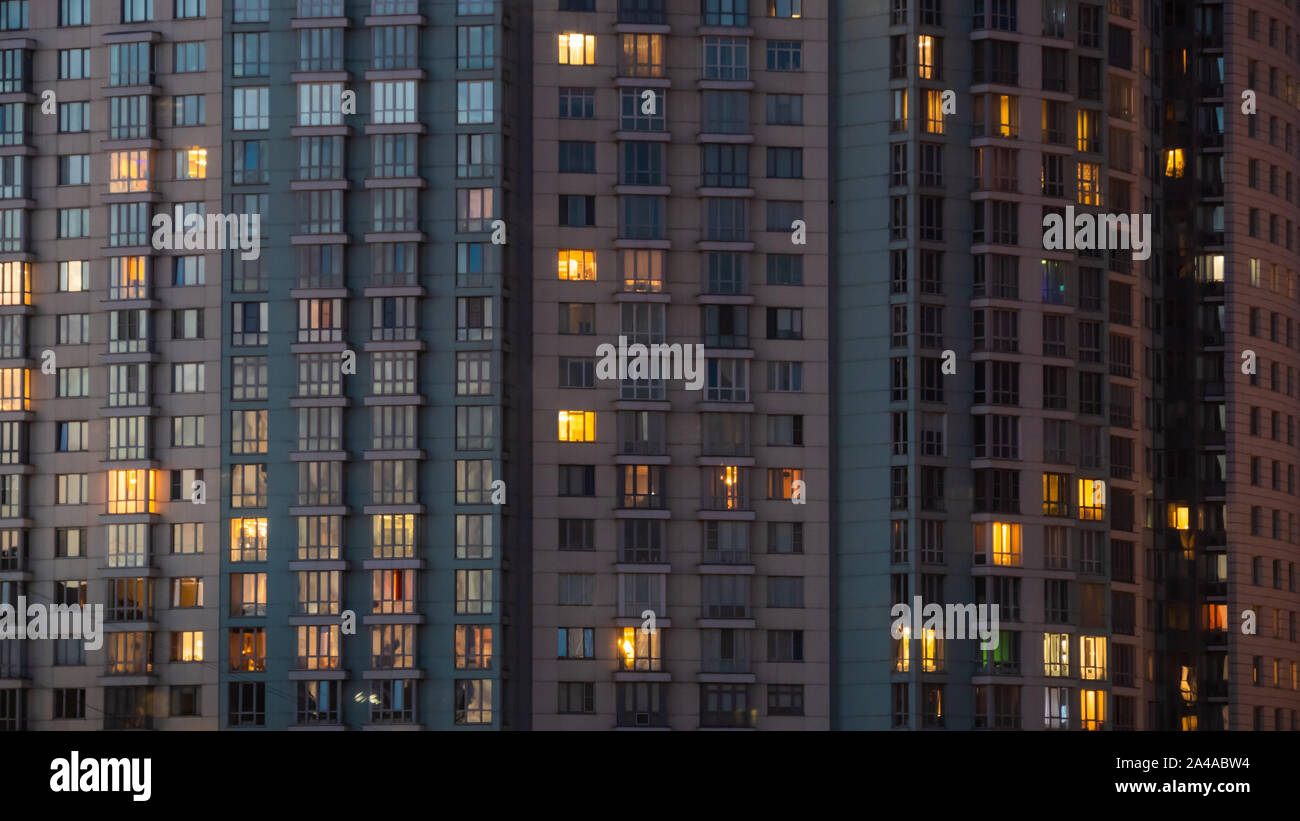 Facade view of living apartment building with glowing windows at dusk ...
