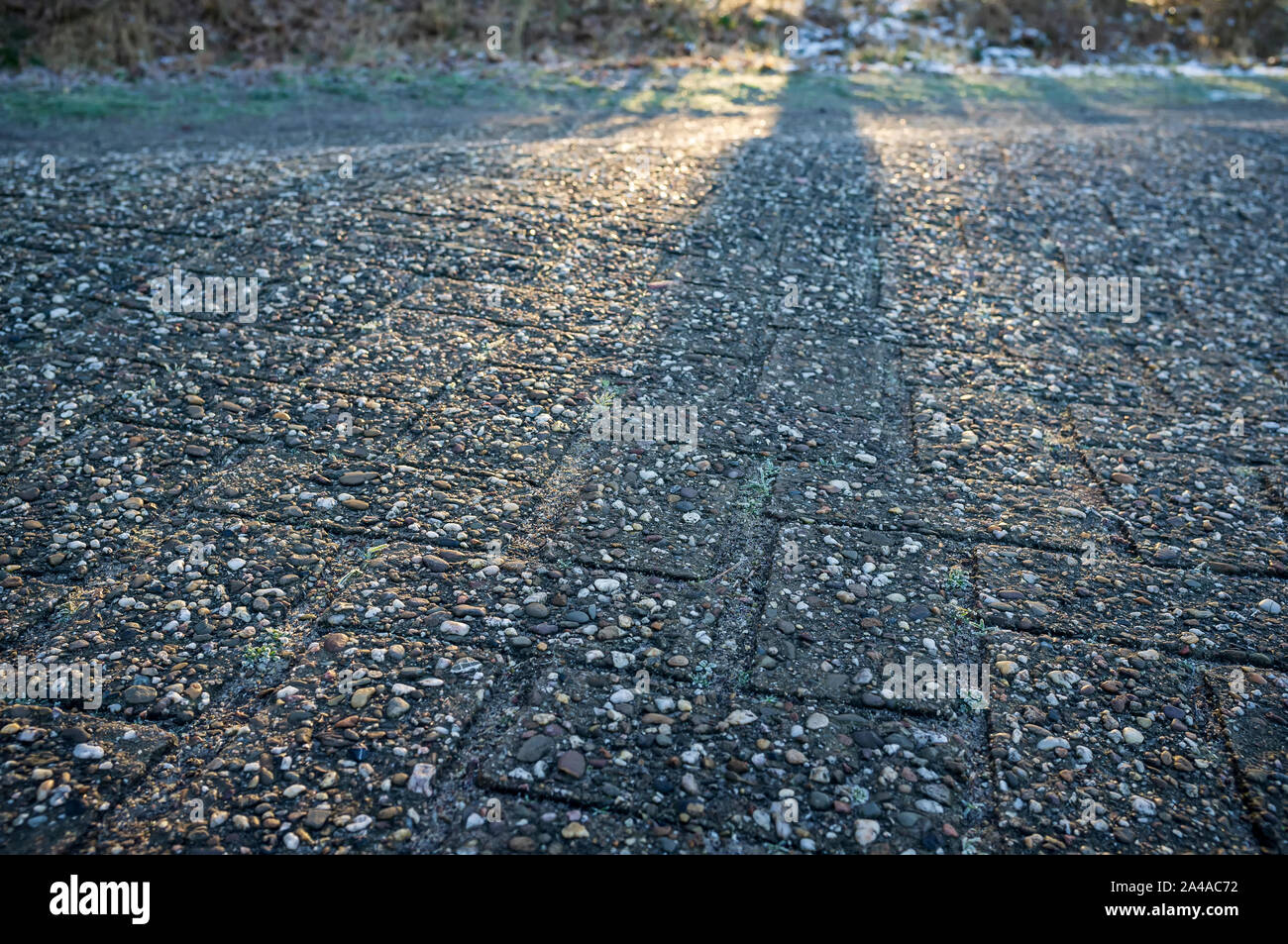 Old, worn patterned asphalt with gravel or pebbles in the rays of the ...