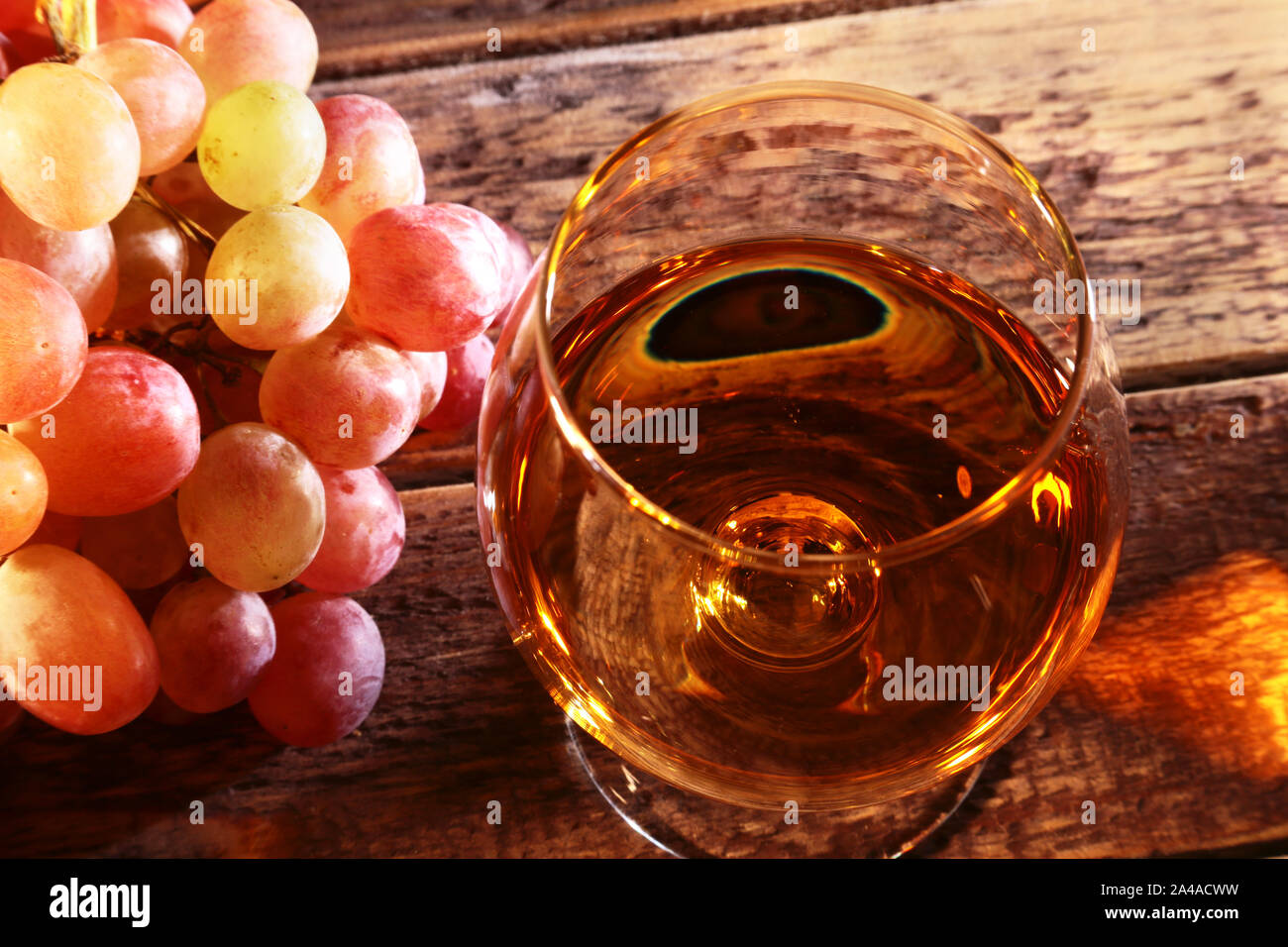 Cognac or Brandy in a glass and fresh grapes, still life in rustic style, vintage wooden ...