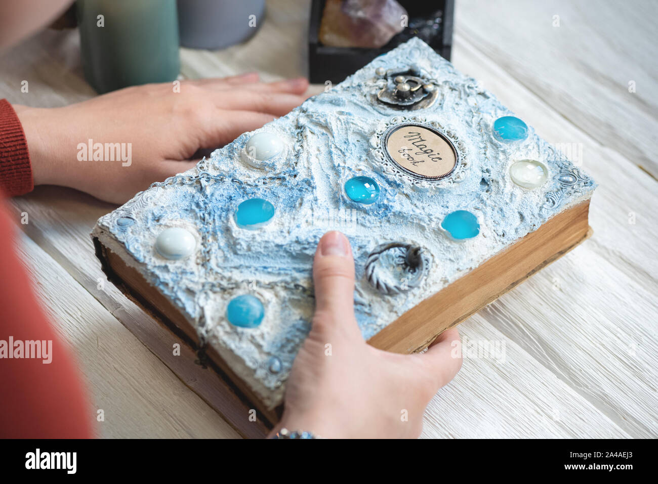 White magic book in a sorceress hand on a white wooden table background ...