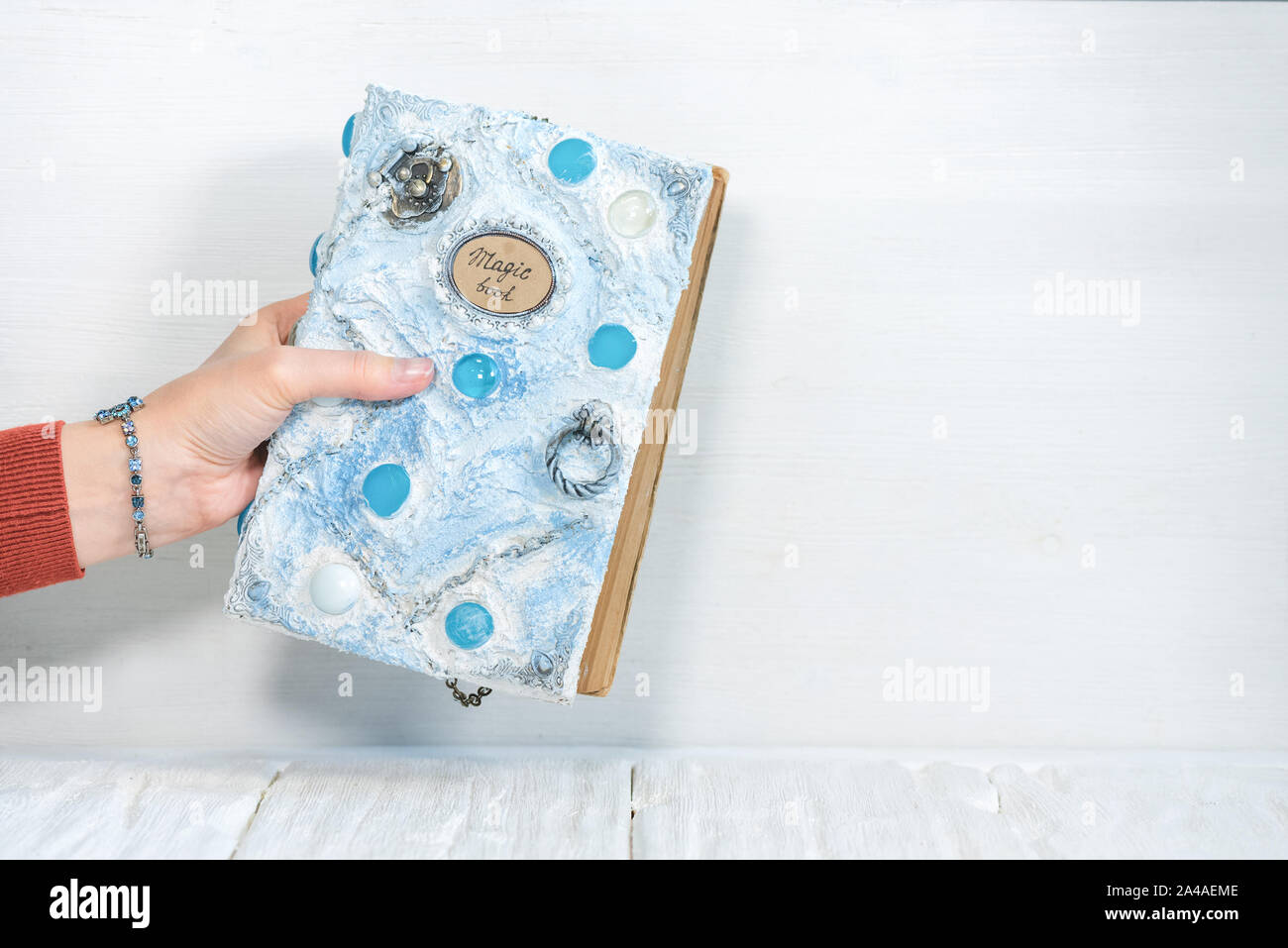 White magic book in a sorceress hand on a white wooden table background ...