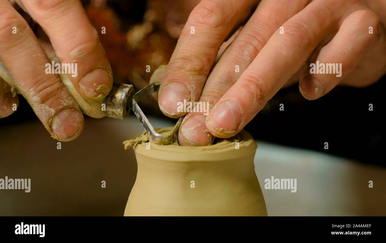 Professional potter shaping mug with special tool in pottery workshop ...