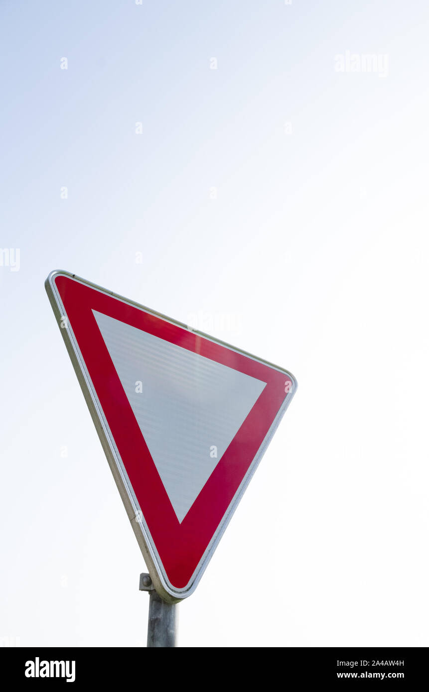 Single triangle road sign in red and white, give way, against blue sky ...