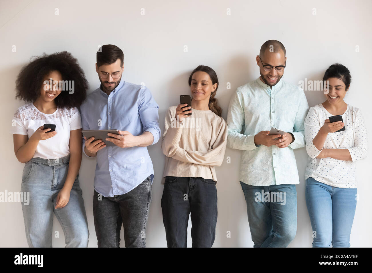 Smiling diverse people using phones, standing in row near wall Stock ...