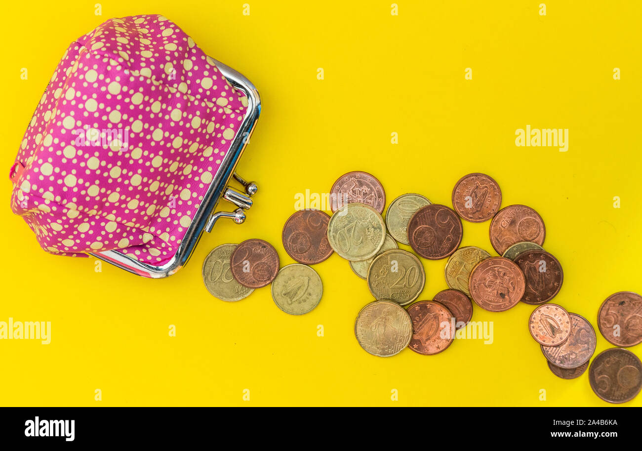 Euro coins spilled out of colourful pink womans purse on yellow ...