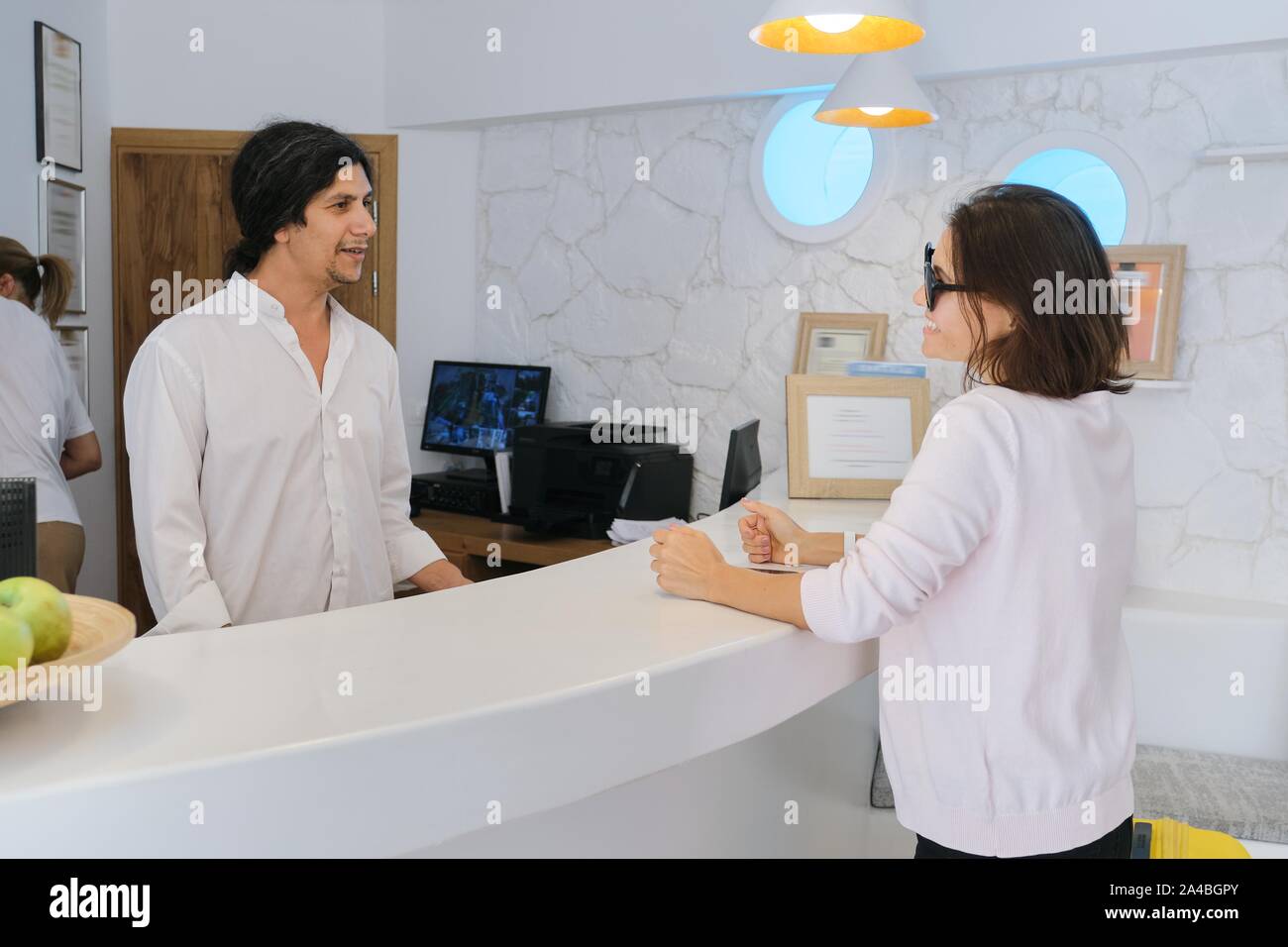 Resort hotel front desk, woman guest talking to man working at ...