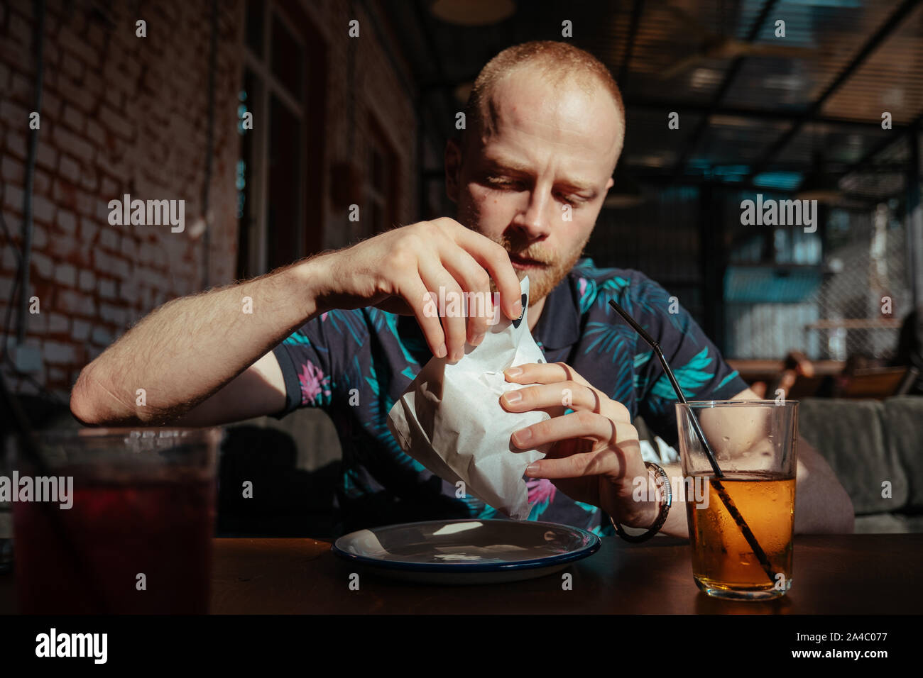The guy holds a juicy hamburger in a summer cafe and lemonade on the ...
