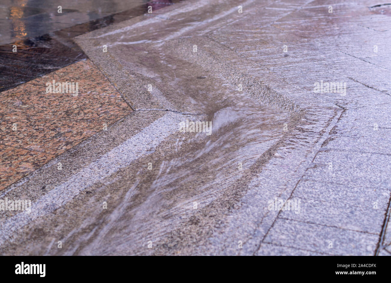 urban street gutter with water flow on tiled sidewalk at rainy day ...