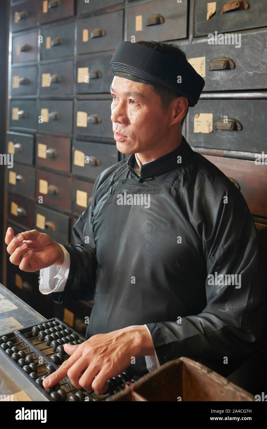 Mature Asian man using abacus when counting price of herbs and medicine ...