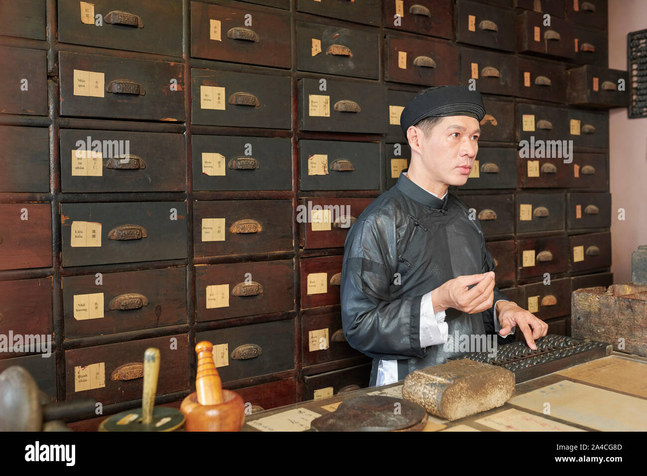 Pensive Vietnamese traditional drugstore worker using abacus when ...