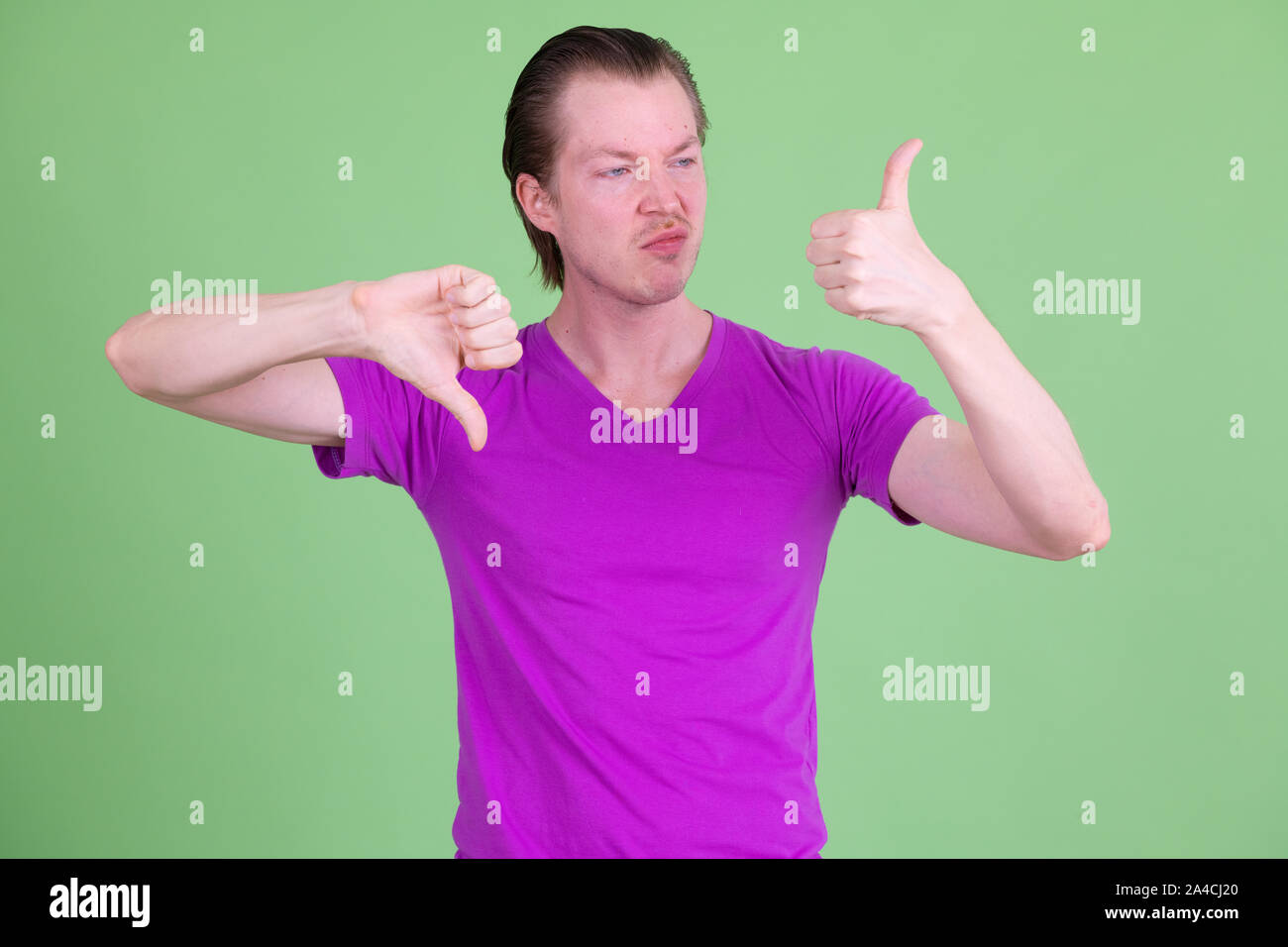 Portrait of confused young man choosing between thumbs up and thumbs ...
