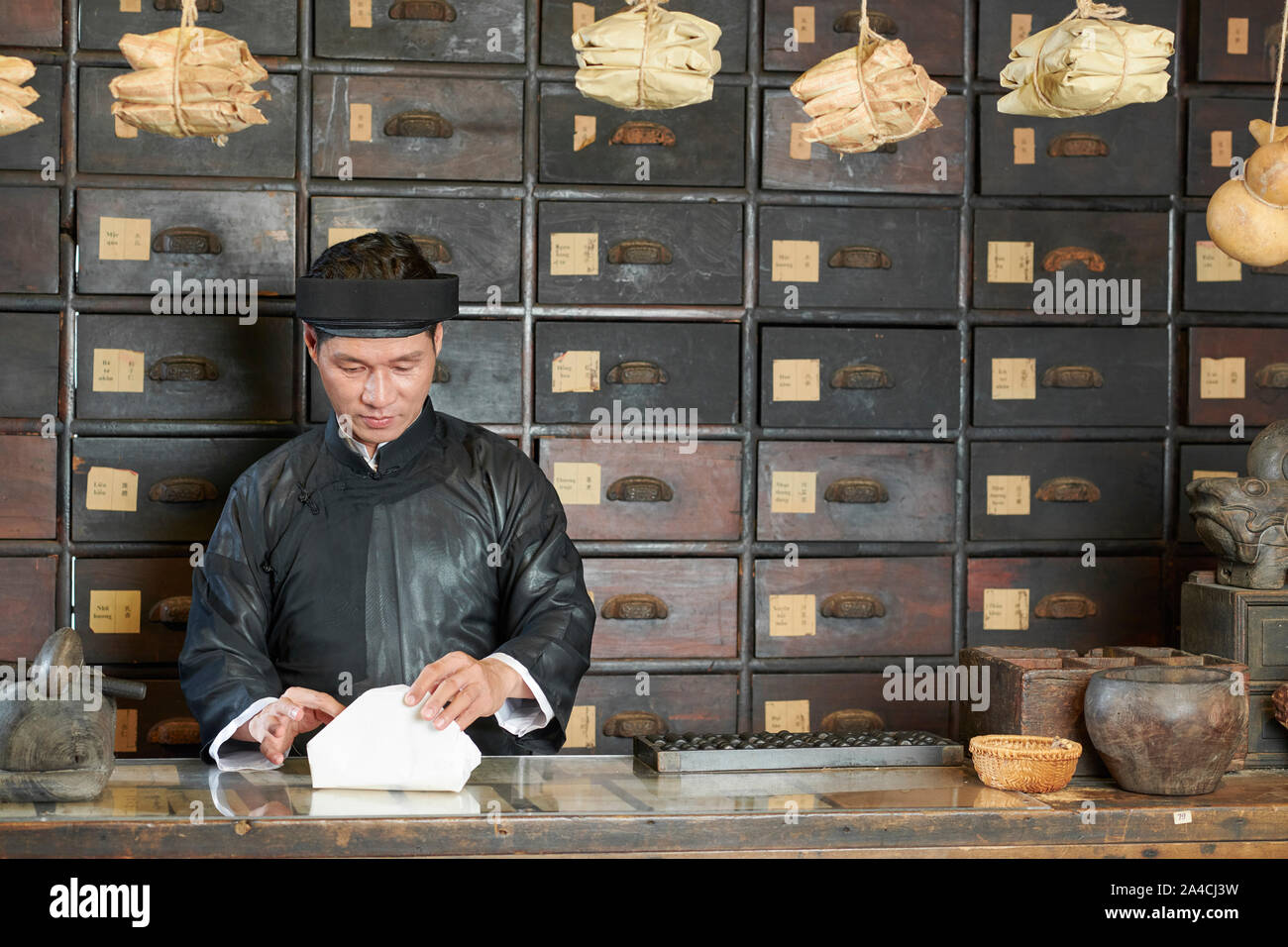 Old Chinese drugstore worker standing at counter and packing order for ...