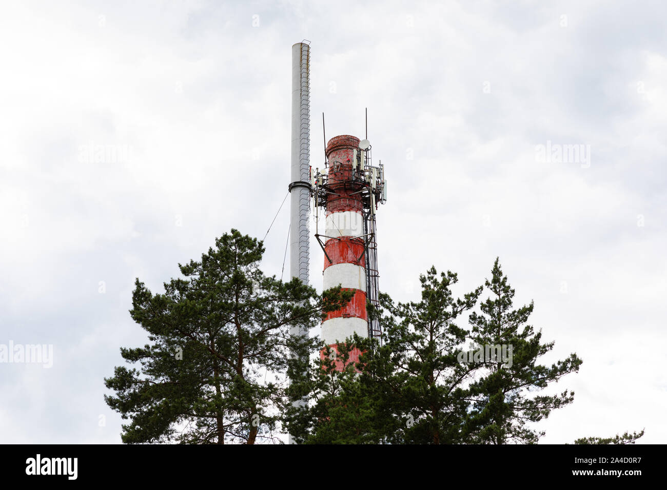 Red white chimney with steel installation on top among trees in blue ...