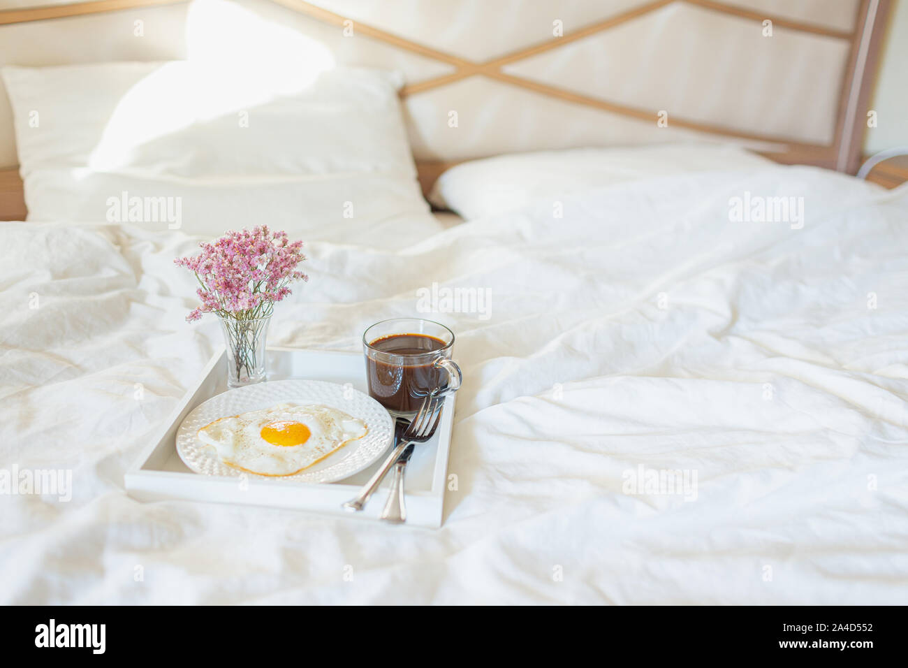 White tray with breakfast on a bed in a hotel room. Fried egg, cup of ...