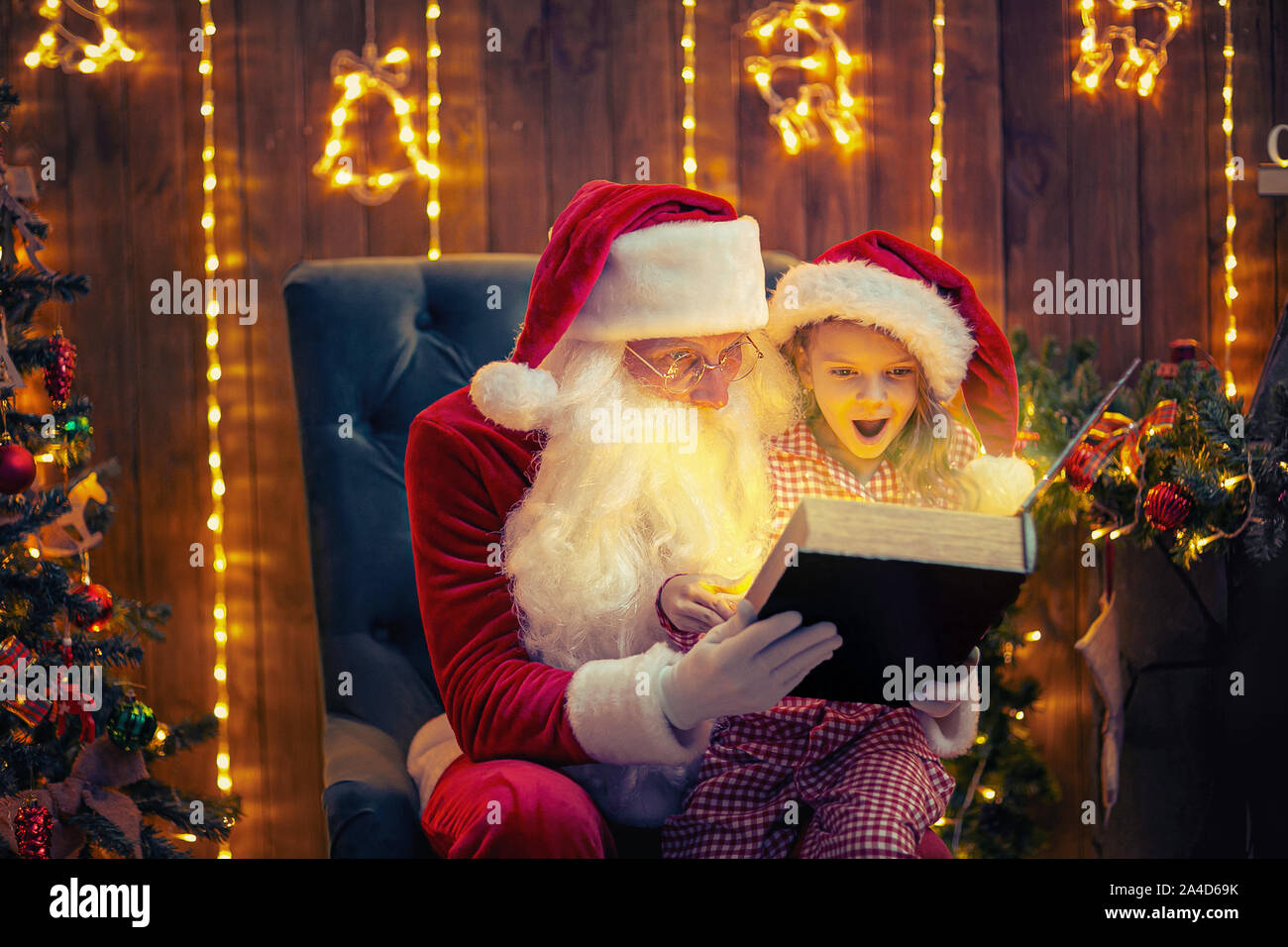 Santa Claus giving a present to a little cute amazed girl in pajama and ...