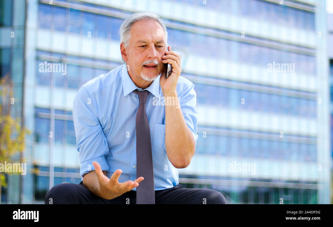 Senior business man yelling at the phone outdoor, sitting on a bench ...