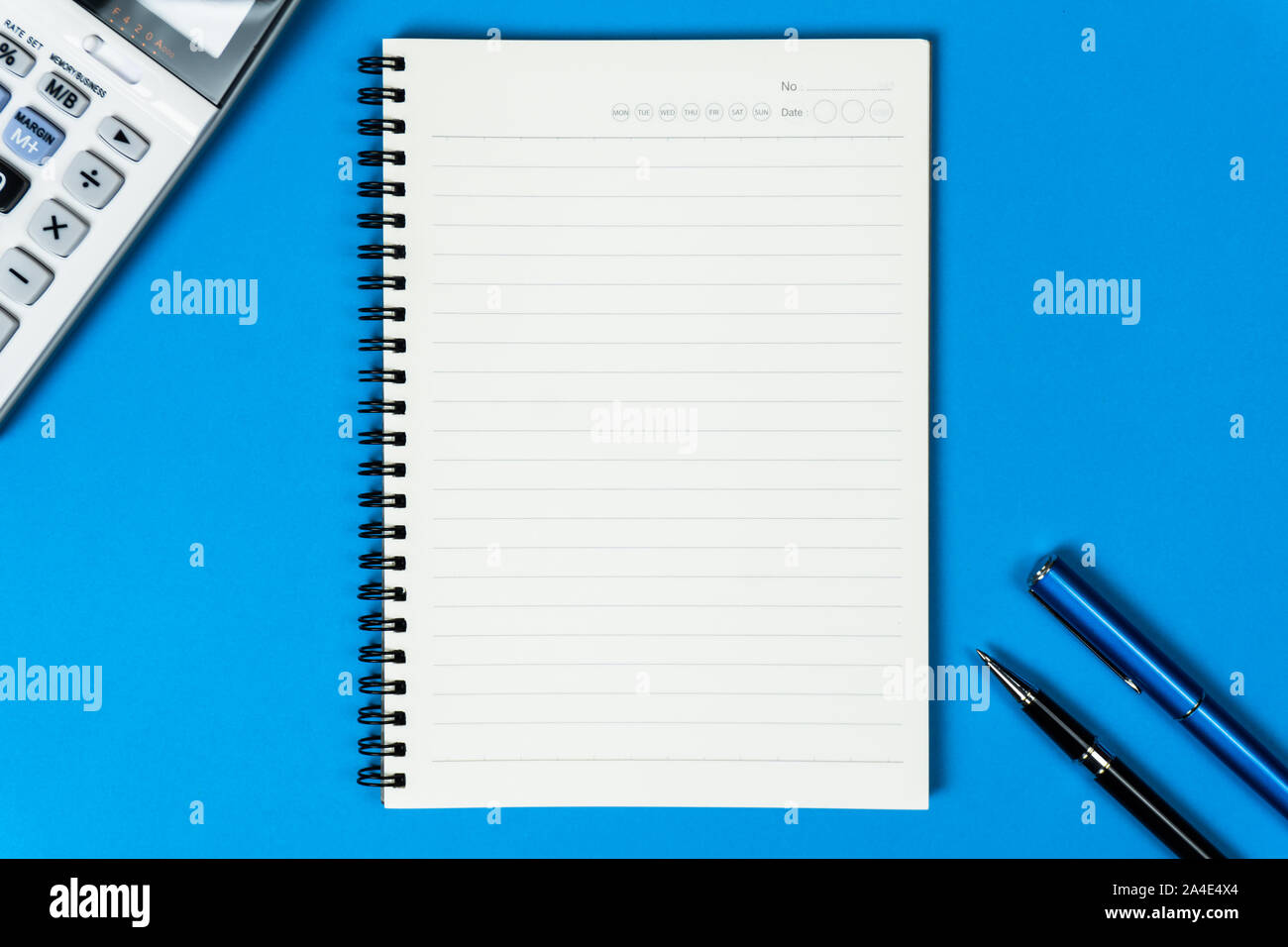 Open notebook with calculator and pen from top view on blue background ...
