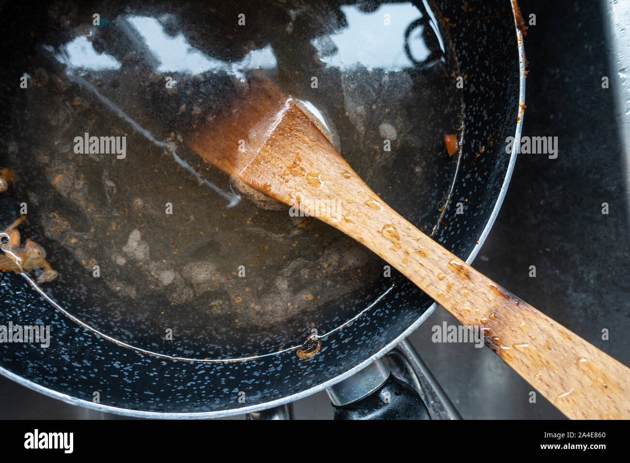 A dirty frying pan and wooden spatula soaking in a kitchen sink Stock ...