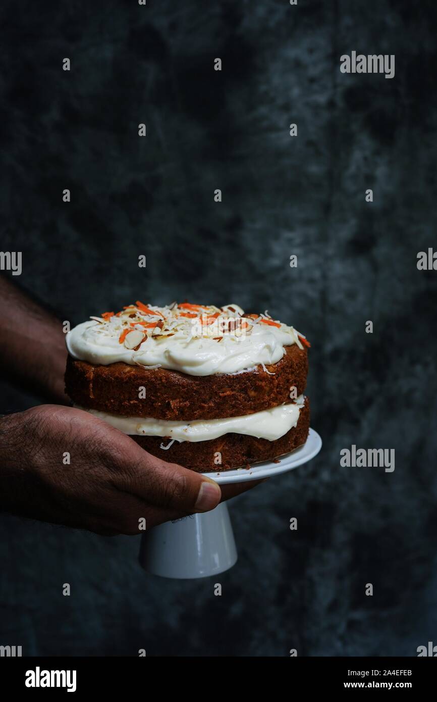 Hand holding cake stand with homemade carrot cake cream cheese frosting ...