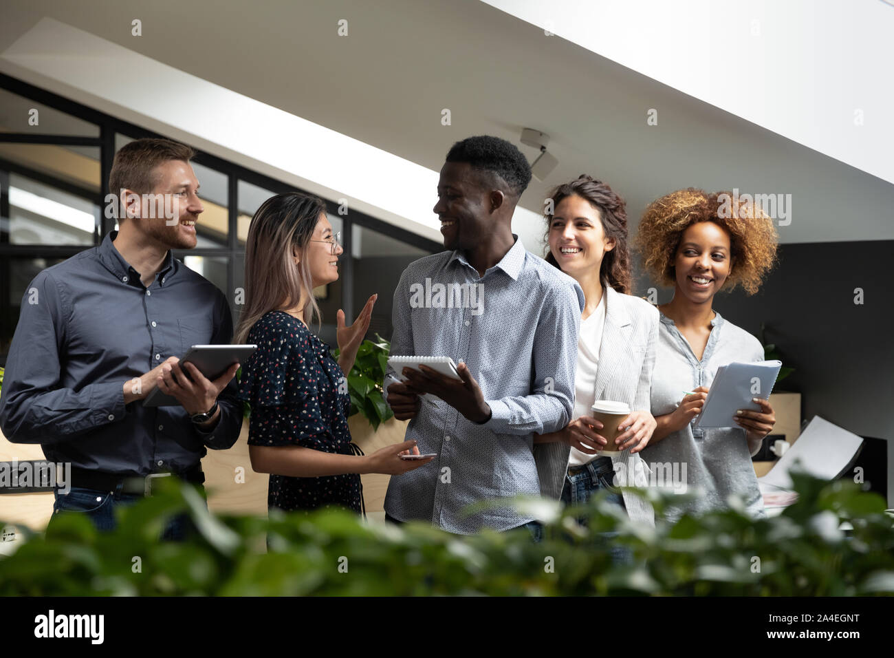 Multiethnic staff standing in modern office hallway talking before ...