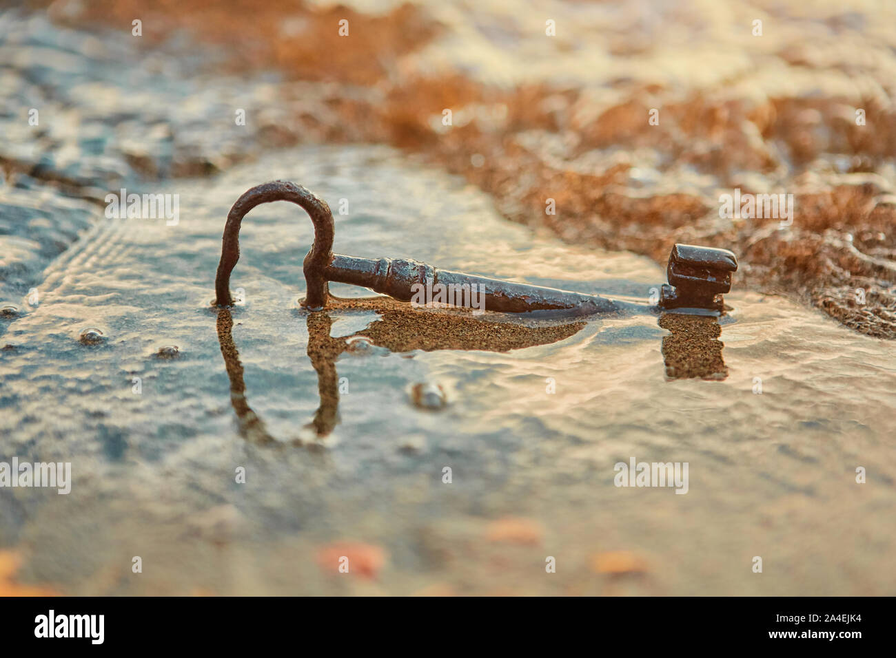 An old rusty lost treasure key, lying in the sand in the surf on the ...