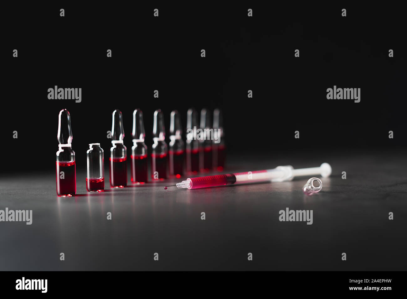 Syringe filled with red liquid from broken ampule on dark background ...