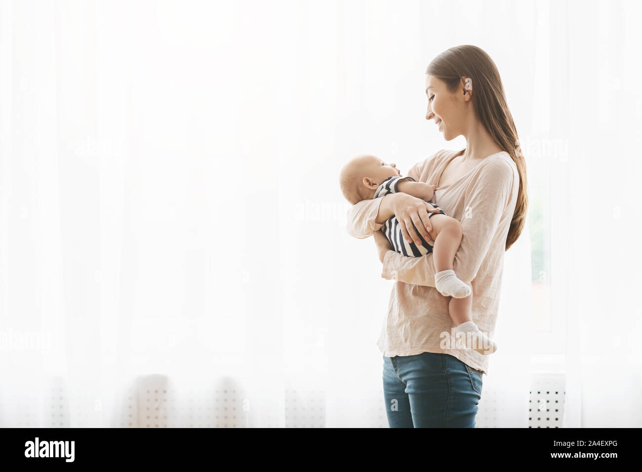 Mother holding her newborn child, standing near window at home Stock ...