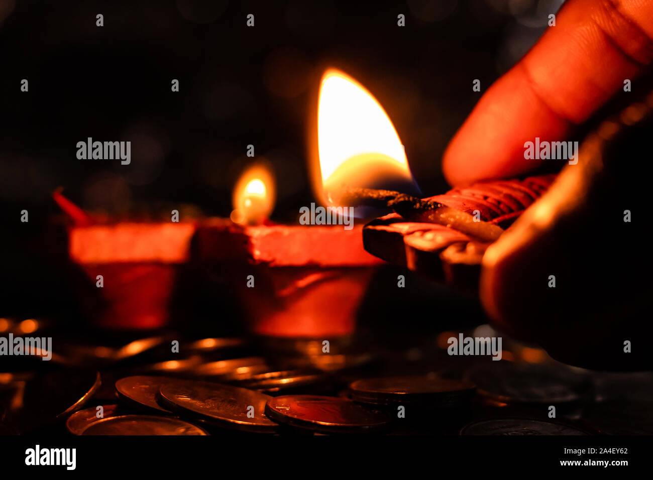 A human hand holding a glowing lamp to light up the other earthen lamps ...