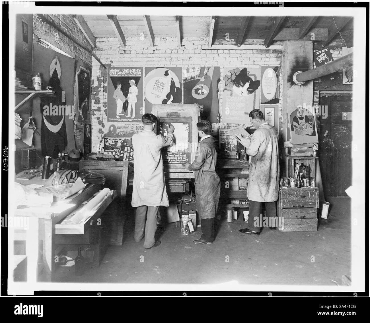Three men working in print shop, numerous posters displayed in ...